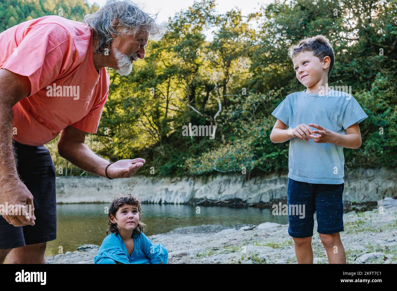 Senior man holding insect while looking at boy spending time with kids ...
