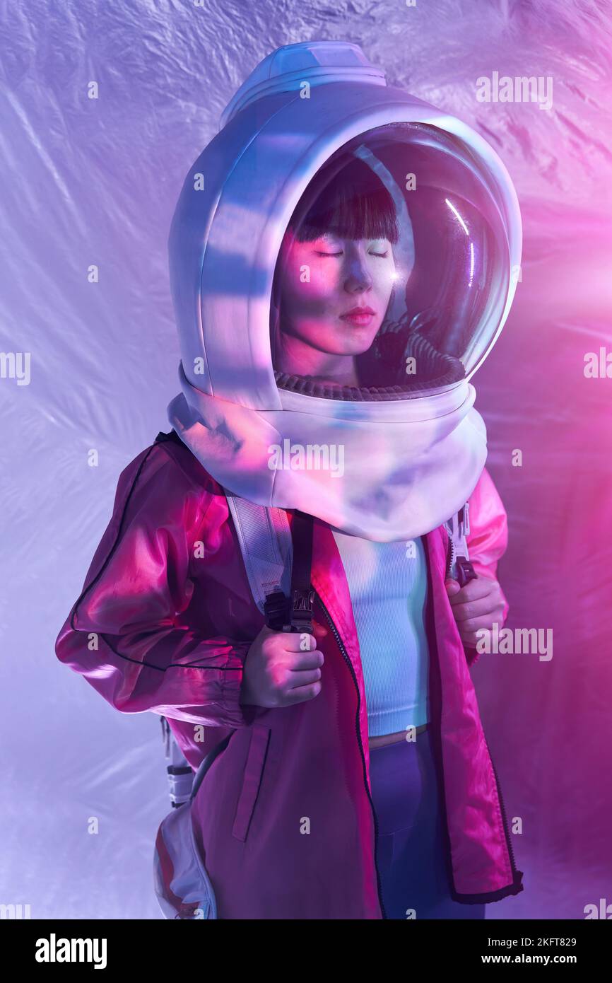 Young Asian female with backpack wearing cosmonaut helmet and closing ...