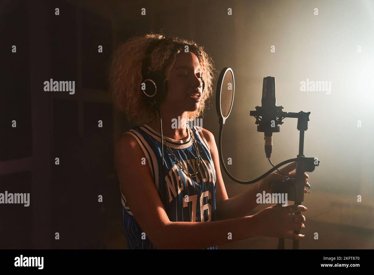 Side view of focused young female singer with Afro hairstyle standing ...