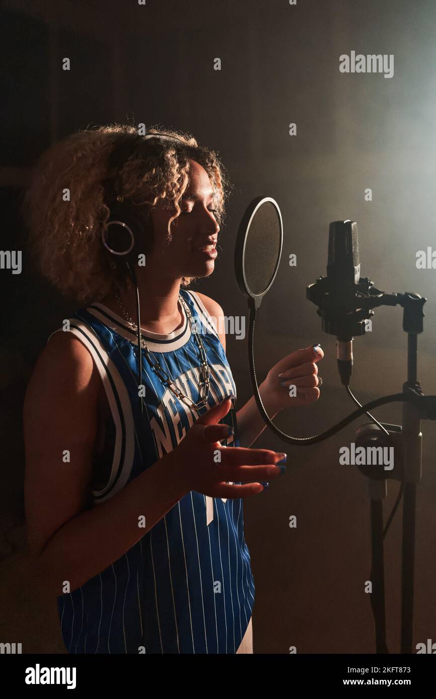 Side view of focused young female singer with Afro hairstyle standing ...