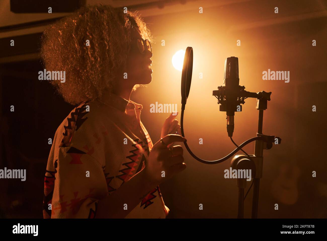 Side view of young female singer with Afro hairstyle standing against ...