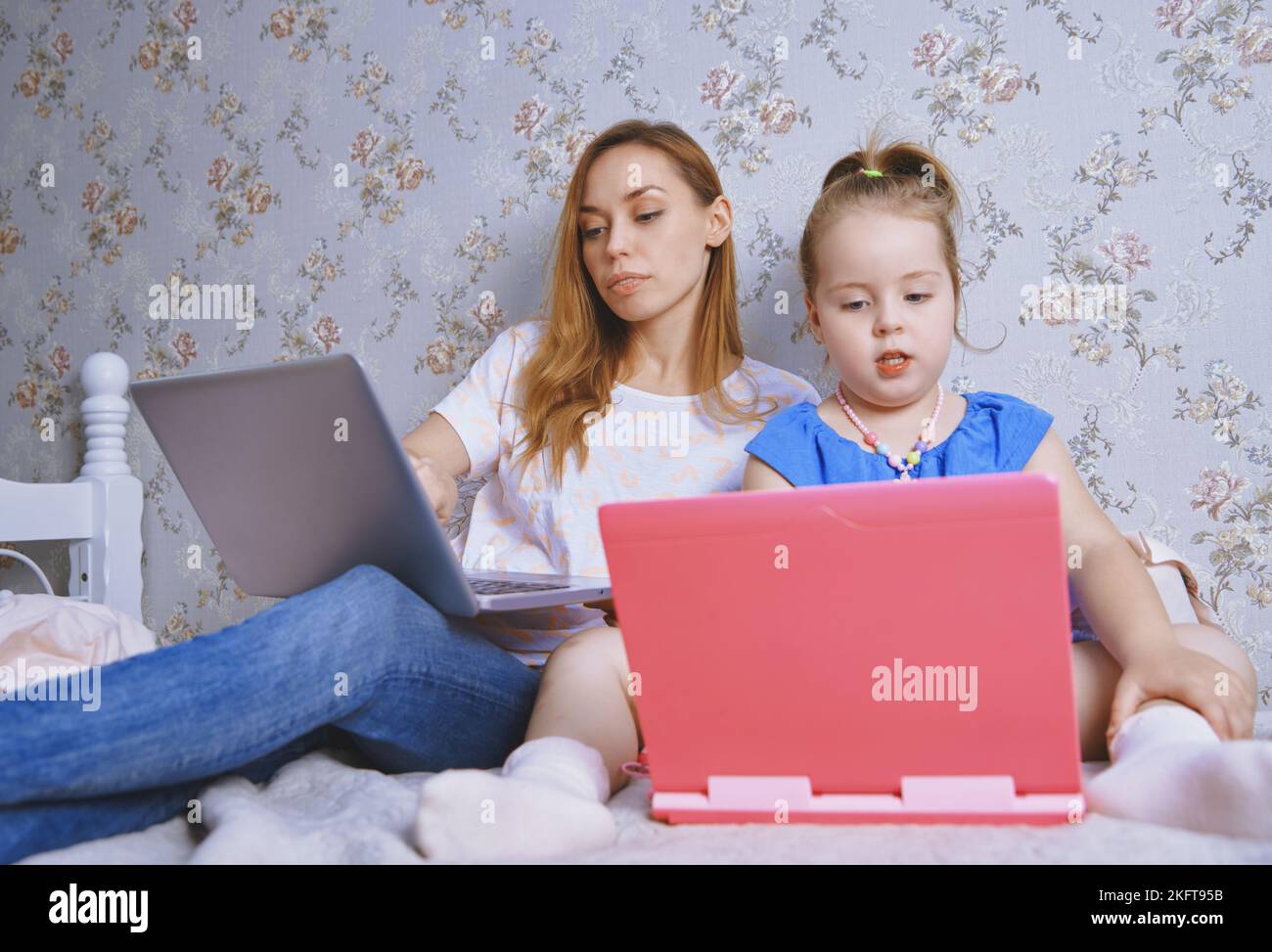 Mother And Daughter Sitting On Bed And Watching Video On Laptops While