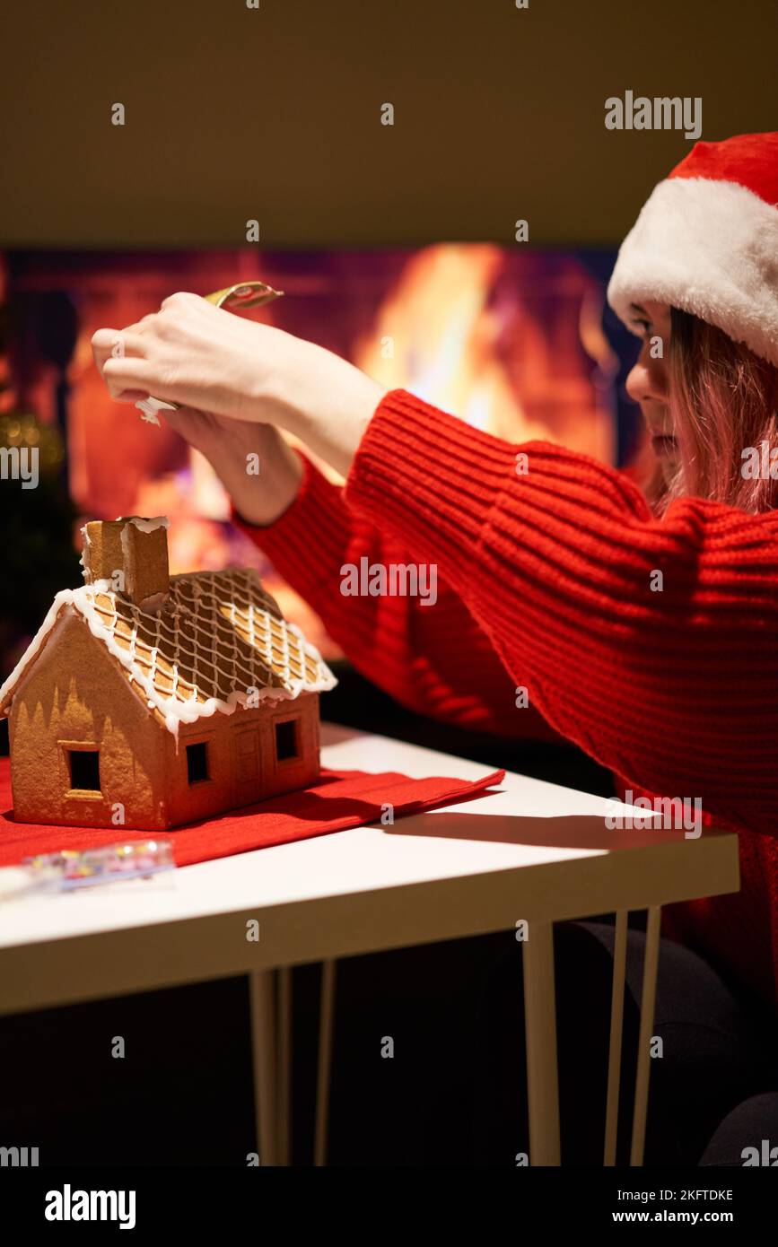 Woman in red hat building gingerbread house. Preparing to celebrate ...