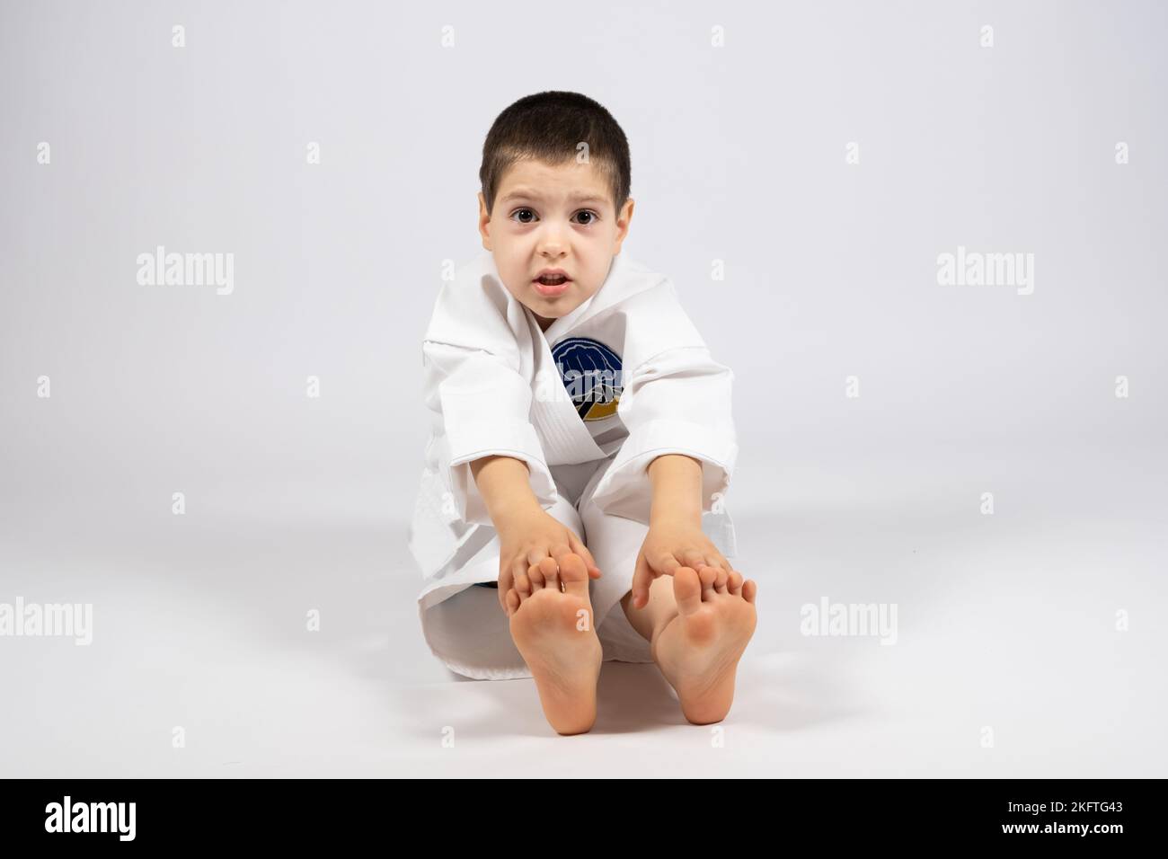 A little boy in a kimono doing karate, stretches his hands to the tips ...