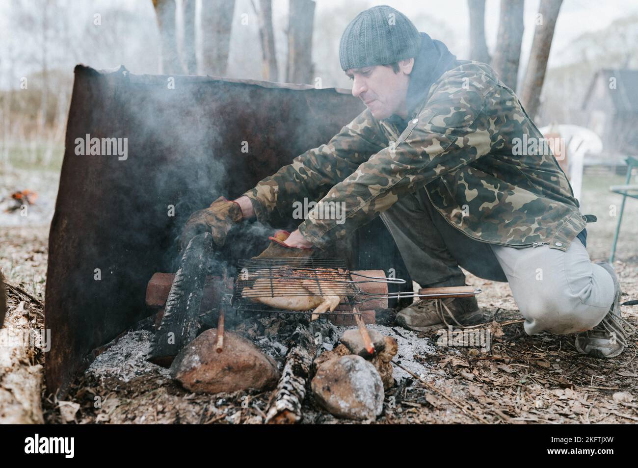 young man survivalist cooks roasts chicken meat food are fried on grill ...