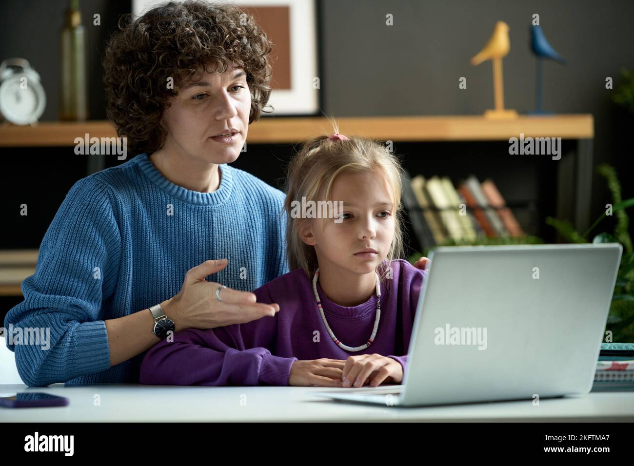 Mother explaining school material to her daughter pointing at laptop ...