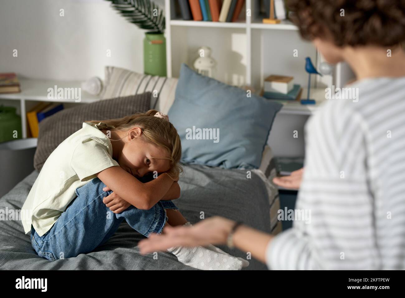 Sad little girl sitting on bed and listening comments from her mother ...