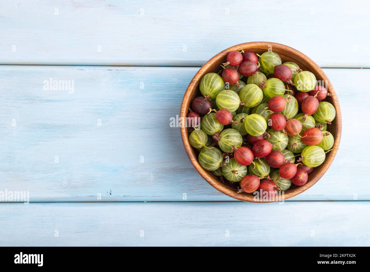 Fresh red and green gooseberry in wooden bowl on blue wooden background ...