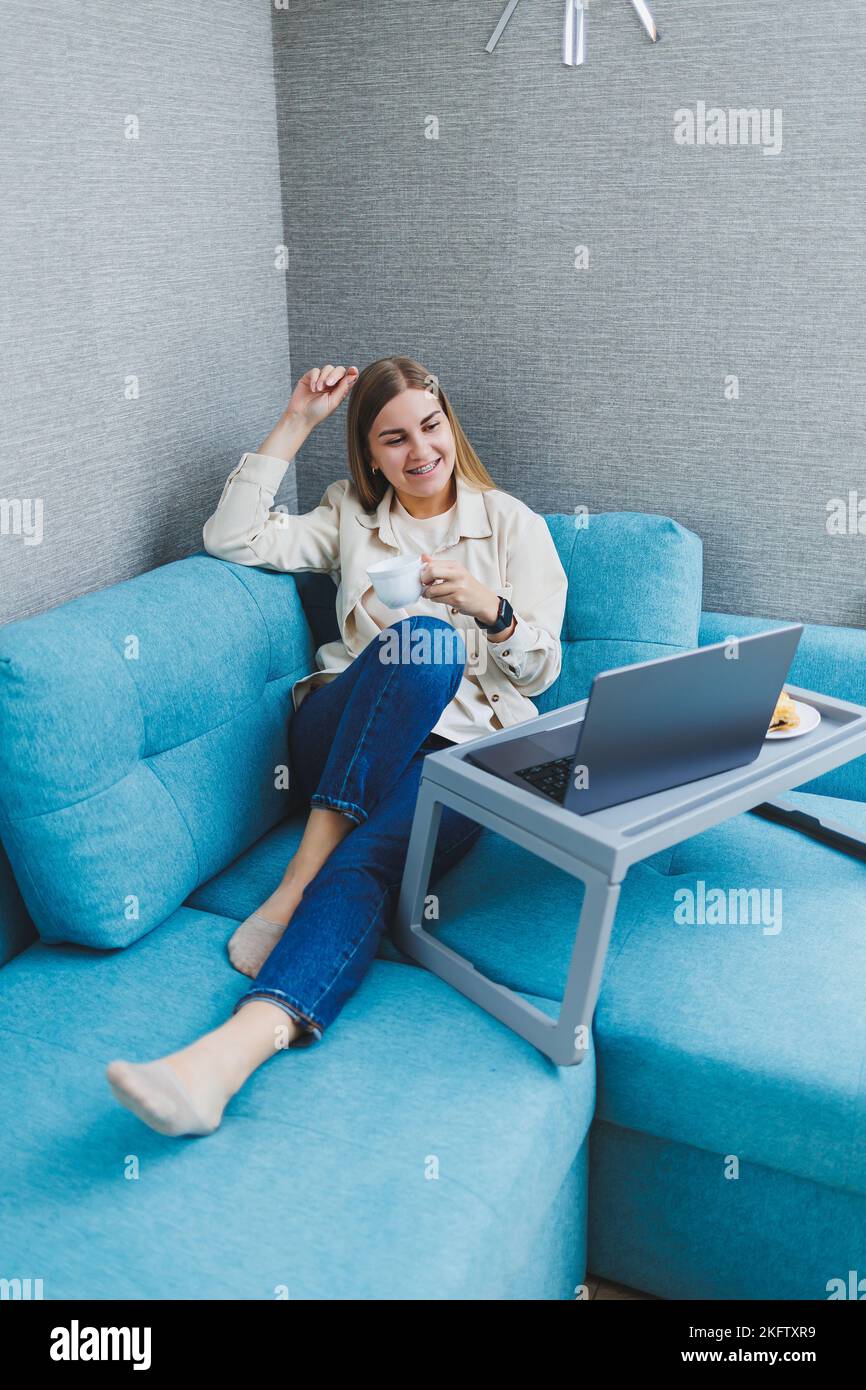 Smiling woman using laptop to check e-mail news online while sitting on ...