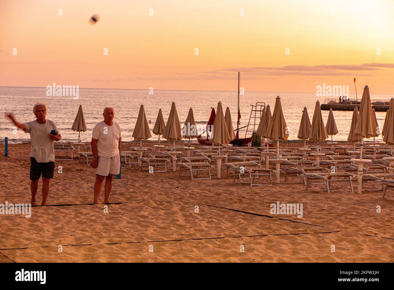 Two mature men enjoy a game of boules on the beach at the end of the ...