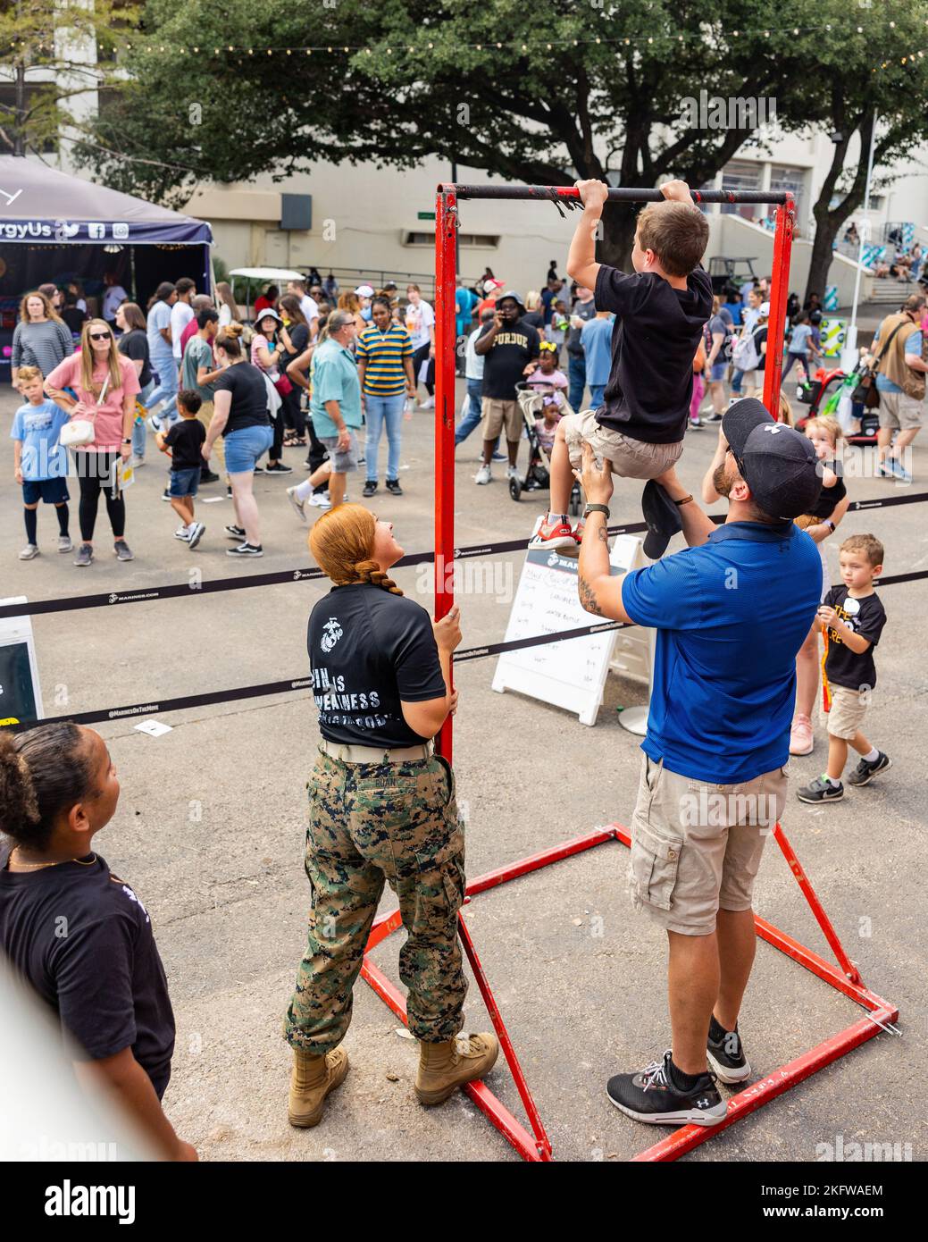 A child, helped by his father, participates in a Marine Corps pull-up ...
