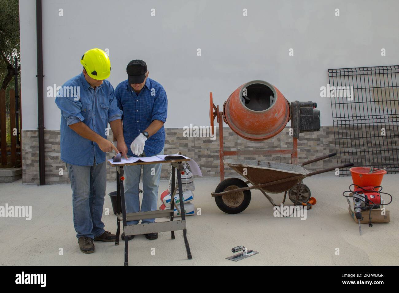 Image of an engineer and construction worker on a construction site as they consult the plan of ...