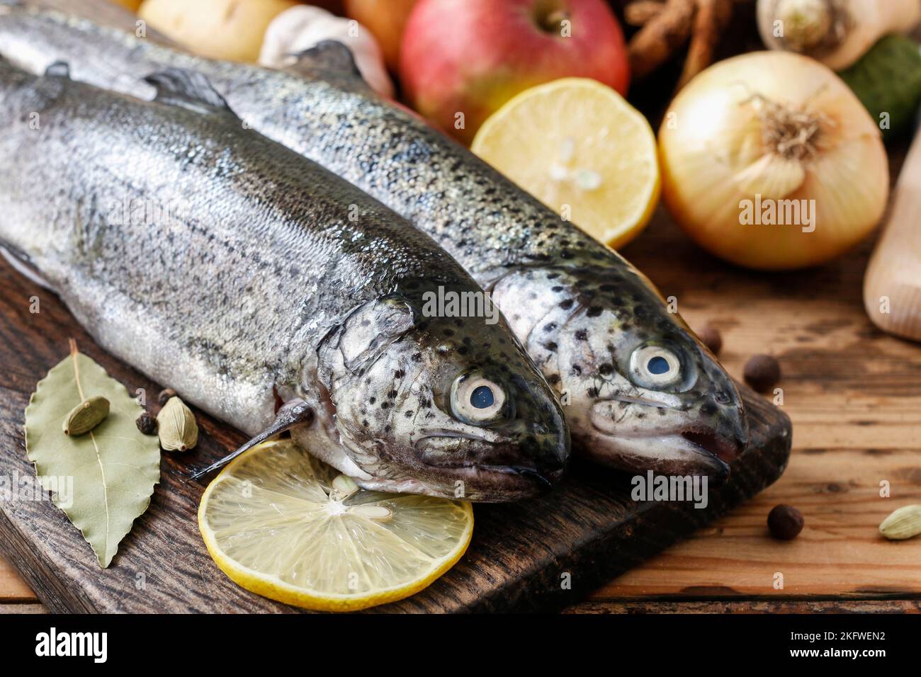 Two rainbow trouts on rustic wooden table among herbs and vegetables ...