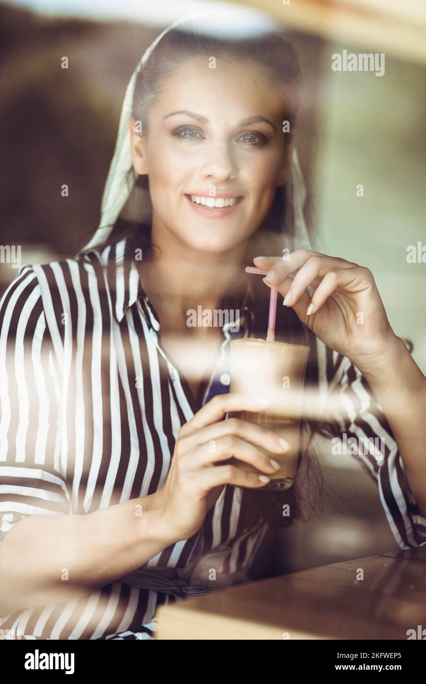 Portrait of a woman in a cafe, drinking coffee. Look through the glass ...
