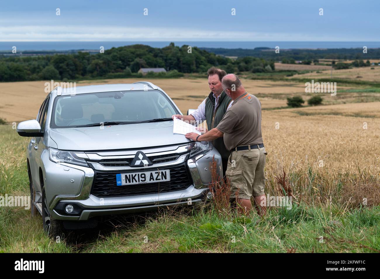 Land agent and farmer, leaning on a pickup, discussing farm management on an arable farm in ...