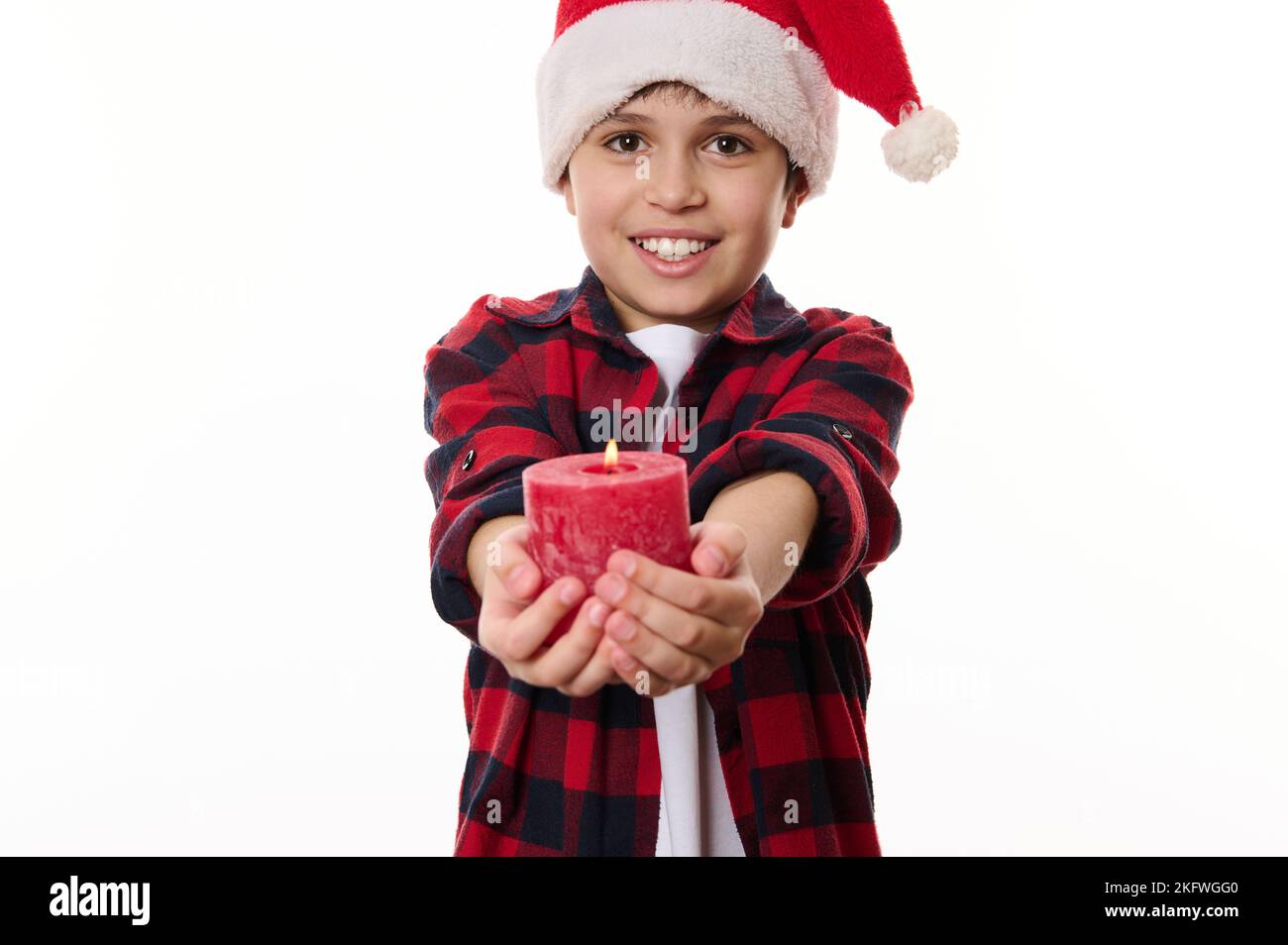 Smiling boy in Santa hat, holding a lit Christmas candle, looking at ...