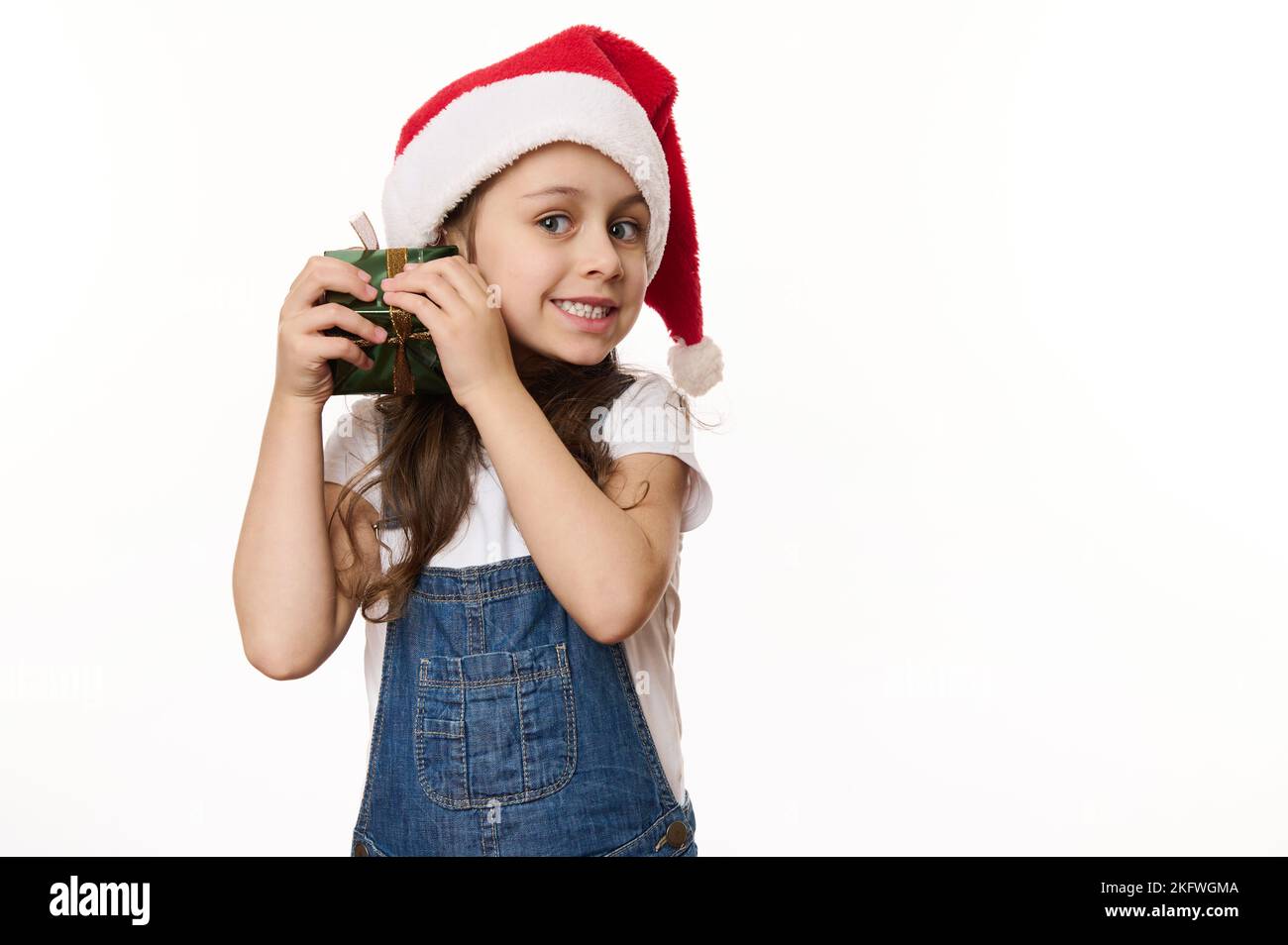 Mischievous little girl in Santa hat, shaking a Christmas present and ...