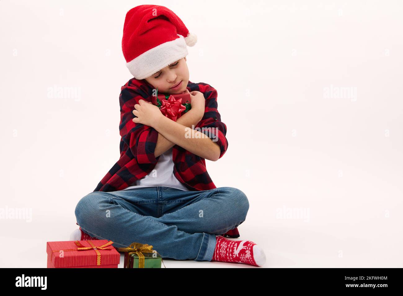 Adorable child boy in Santa hat, gently hugs a Christmas gift, isolated ...