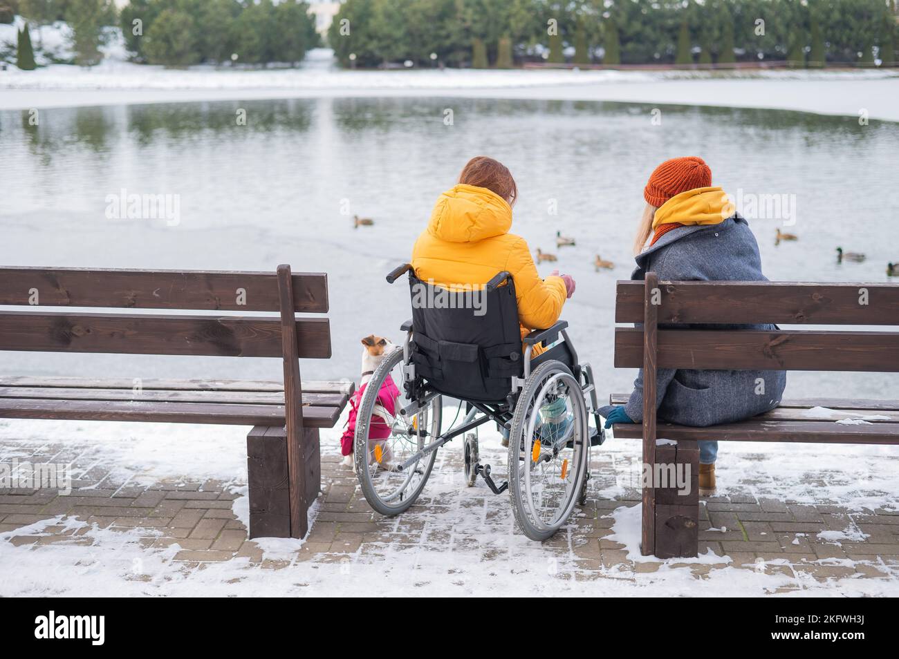 Caucasian woman in a wheelchair and her friend are sitting by the lake ...