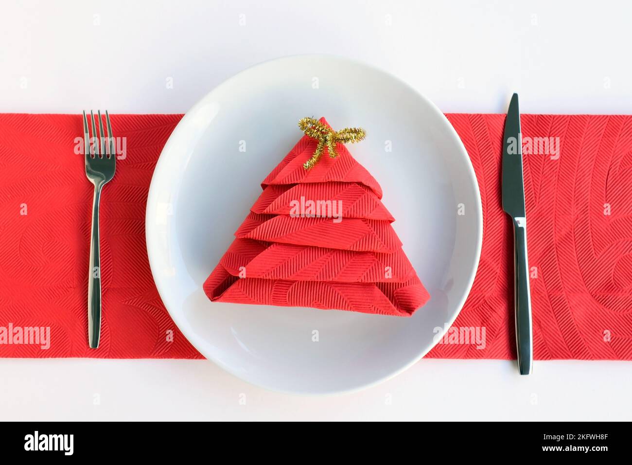 Red napkin folded in pine tree shape in plate with cutlery set ...