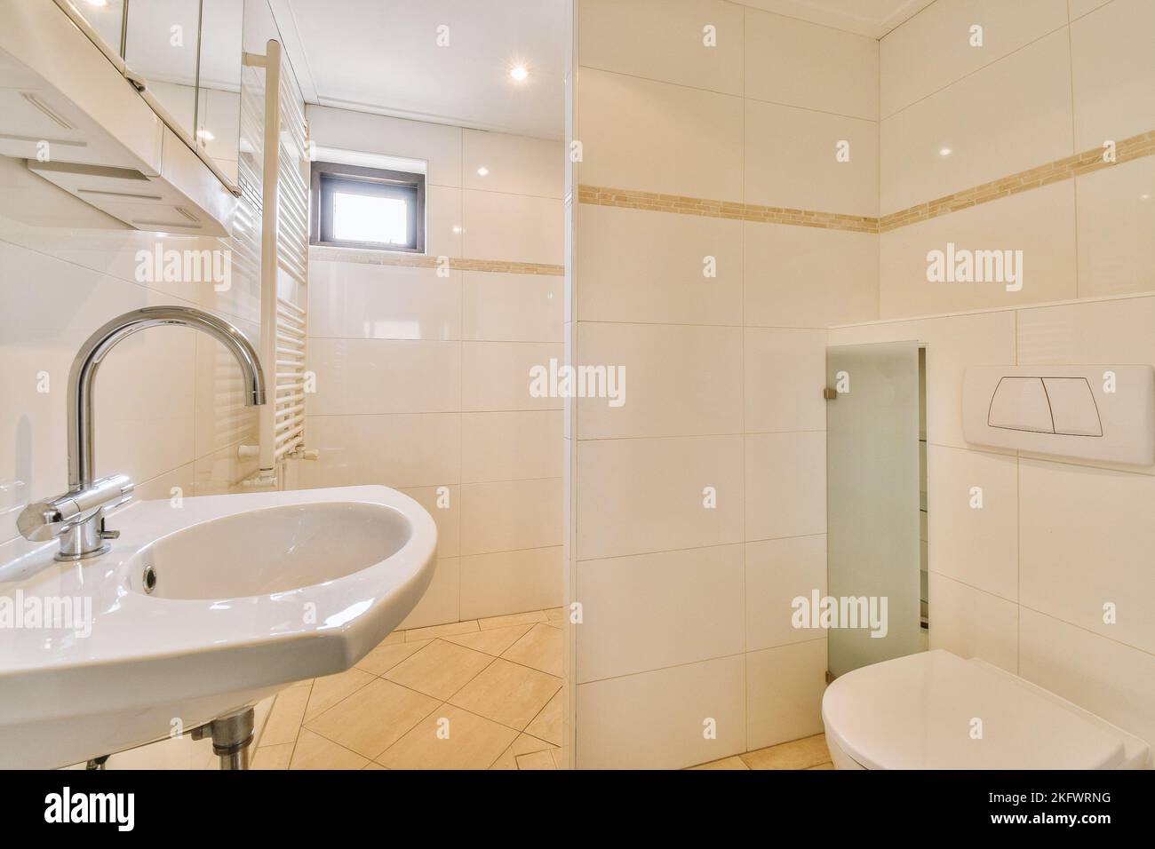 Flush toilet located between sink and shower in small tiled bathroom of ...