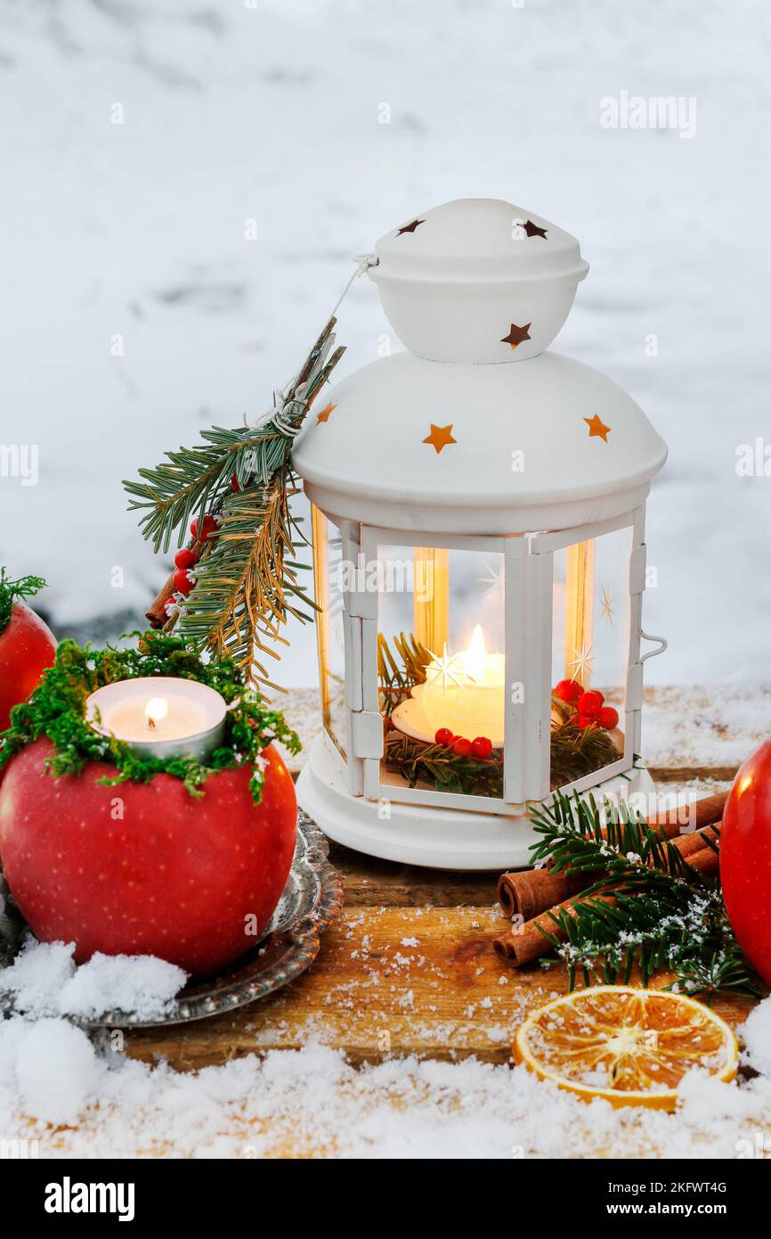 White lantern in winter garden, apples, fir and snow on wooden bench ...