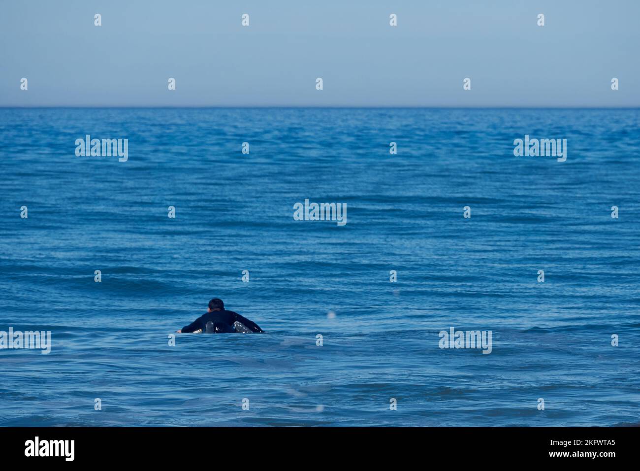 A beautiful shot of a surfer swimming out to waves on the blue sea ...