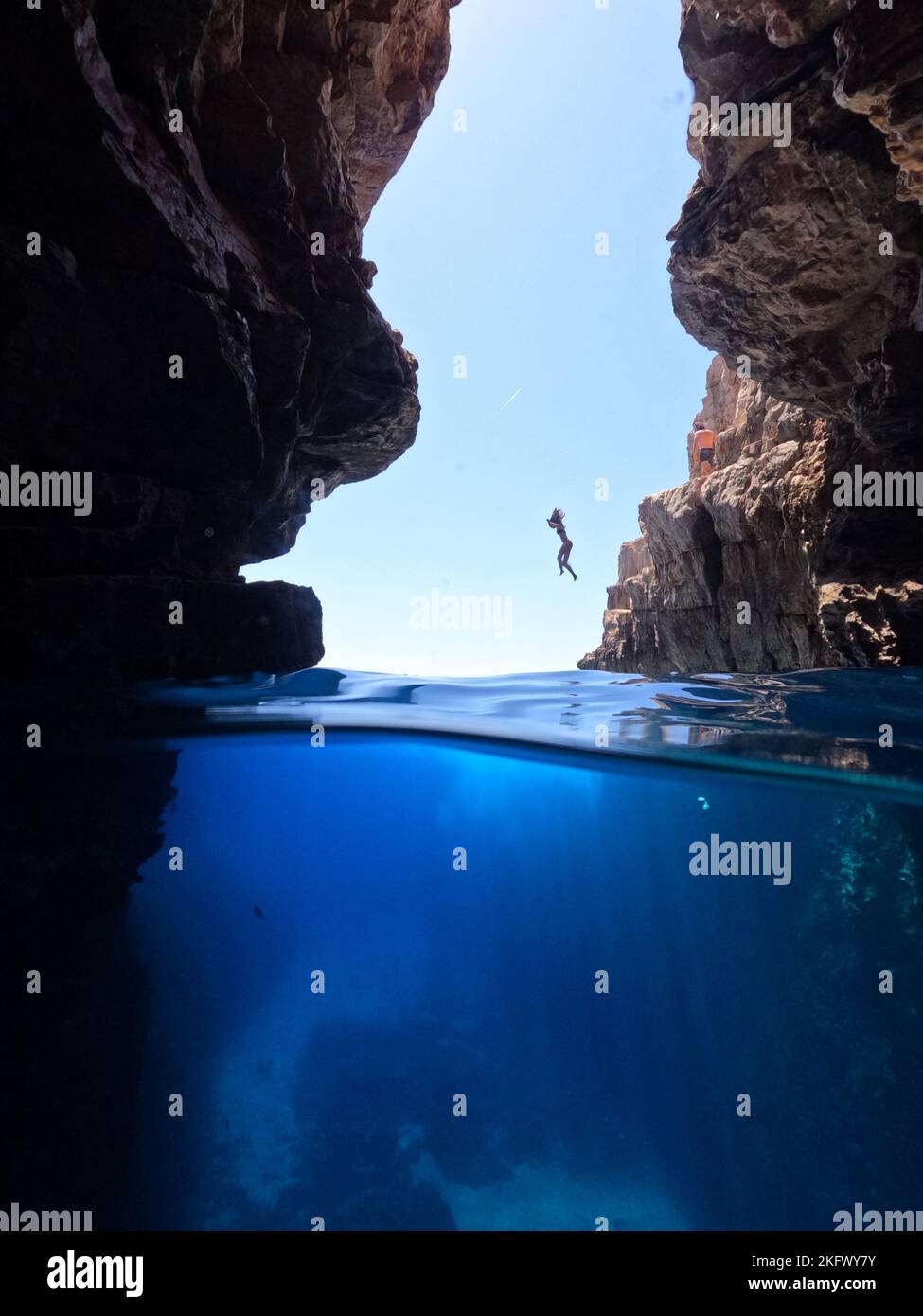 A scenic vertical shot of a person jumping from a rocky cliff into the ...