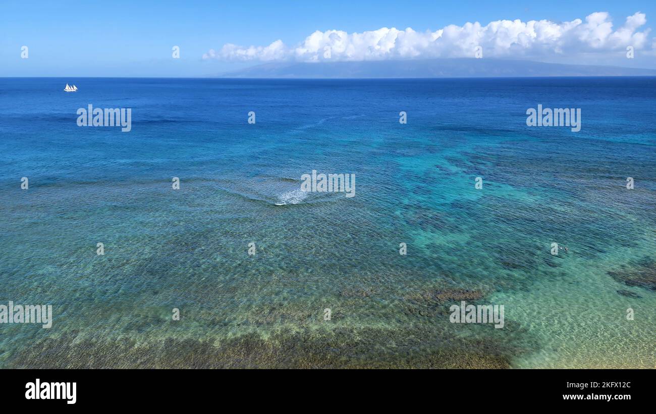 A high-angle of Hawaii ocean with reef and sailboat on the horizon ...