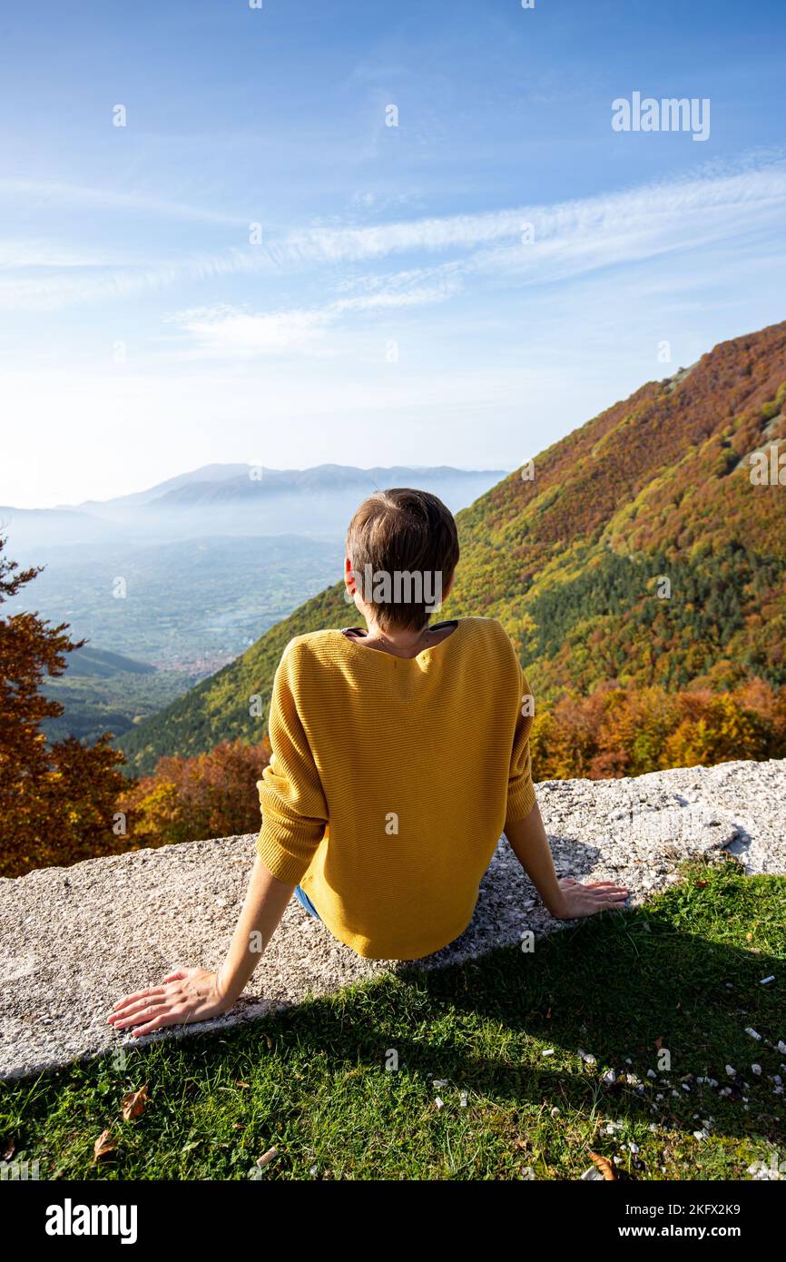 Young woman is sitting and looking at autumn landscape in Italy. Woman ...