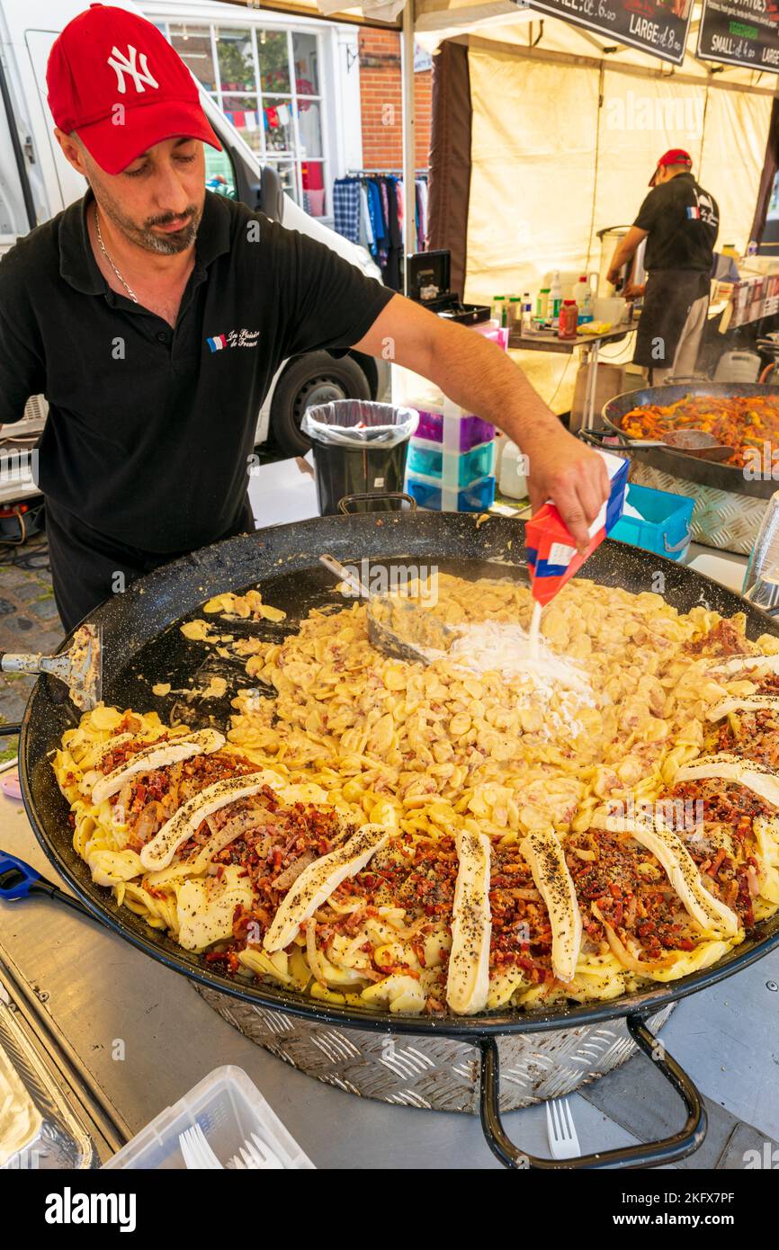Close up a man pouring a carton of cream into a large skillet pan of ...