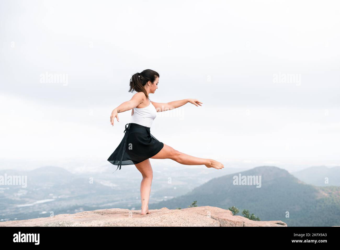 Caucasian mature woman exercising barefoot on the big rock of the ...