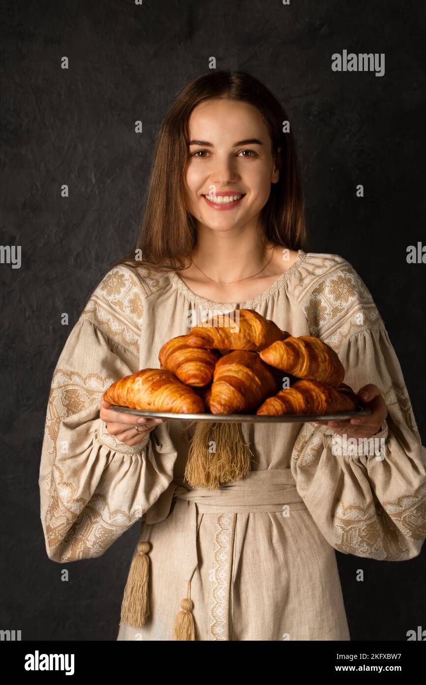 Ukrainian woman in national dress holds a tray with rosy croissants on ...