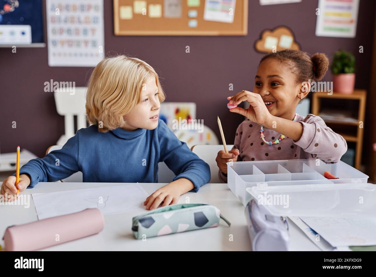 Cute primary school learner using pencil sharpener while sitting by ...