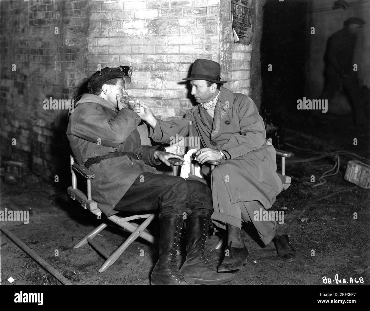 Director MICHAEL CURTIZ lights cigarette for PAUL MUNI on set candid ...