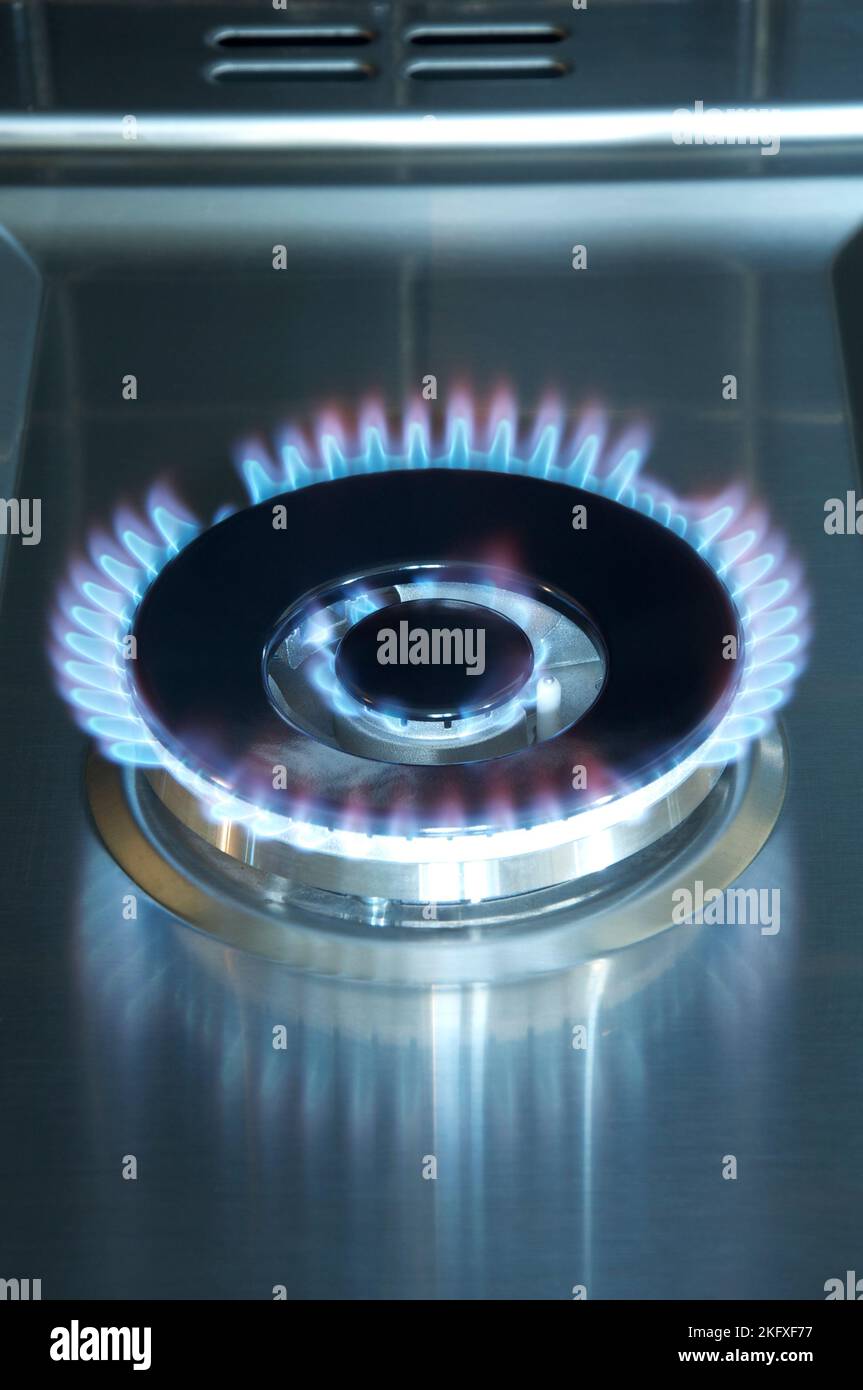 Blue flames burn from a lit gas jet on the hob of a kitchen cooker ...
