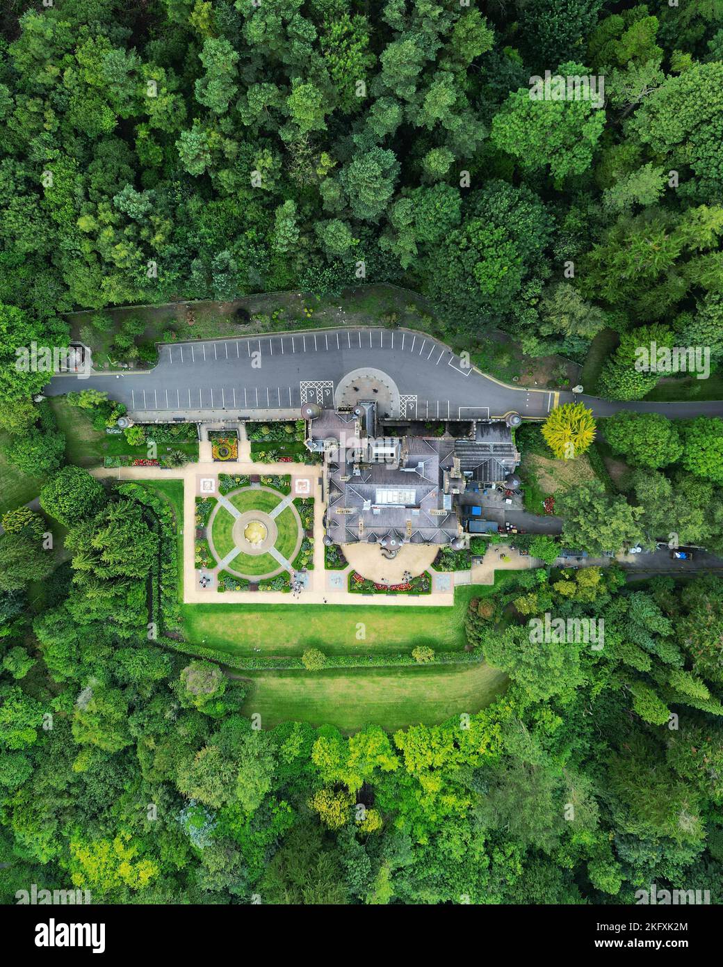 A vertical top shot of a building roof surrounded by gardens and dense ...