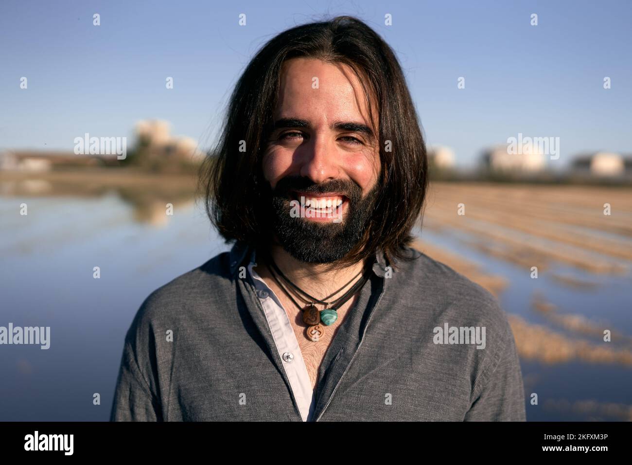 Caucasian young man with beard and long hair standing smiling baring ...