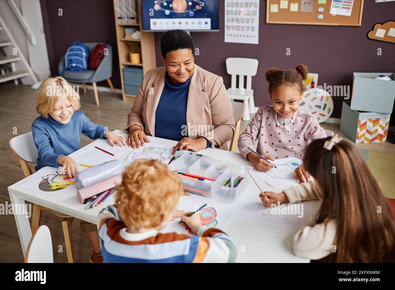 Group of intercultural happy little learners and African American mature teacher interacting at ...