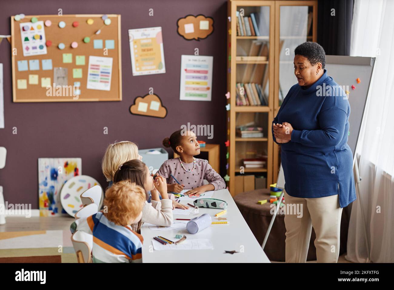 Confident mature teacher in casualwear making presentation to cute ...
