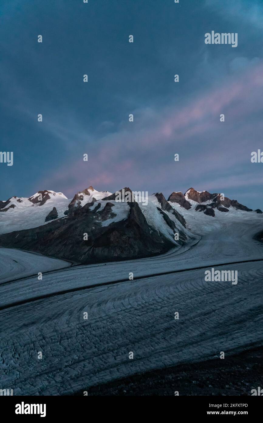 A vertical shot of the snowy rocky mountains under an evening sky in ...