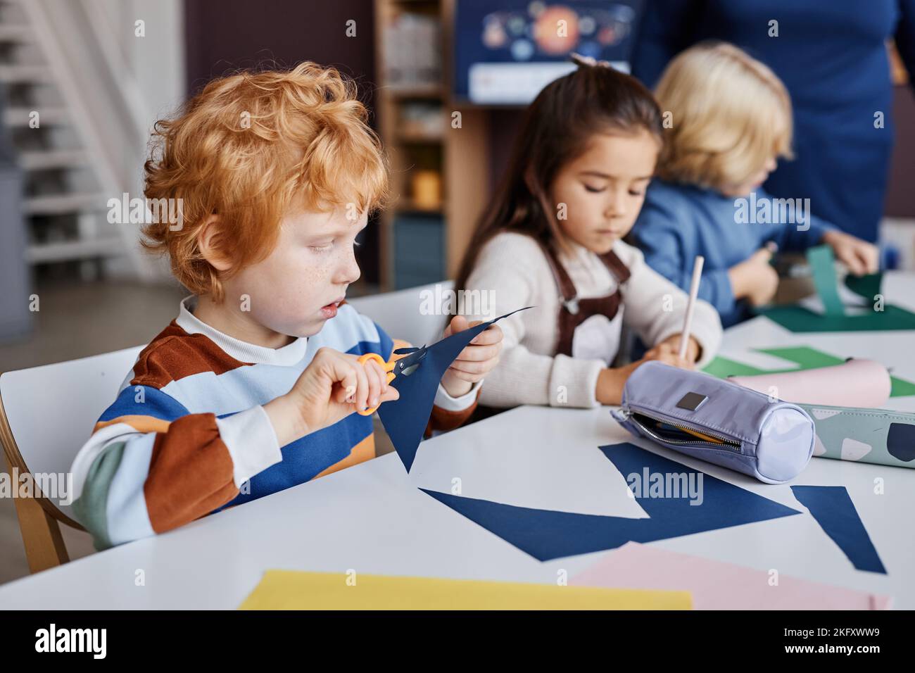 Cute diligent schoolboy with scissors cutting holes for eyes in paper ...