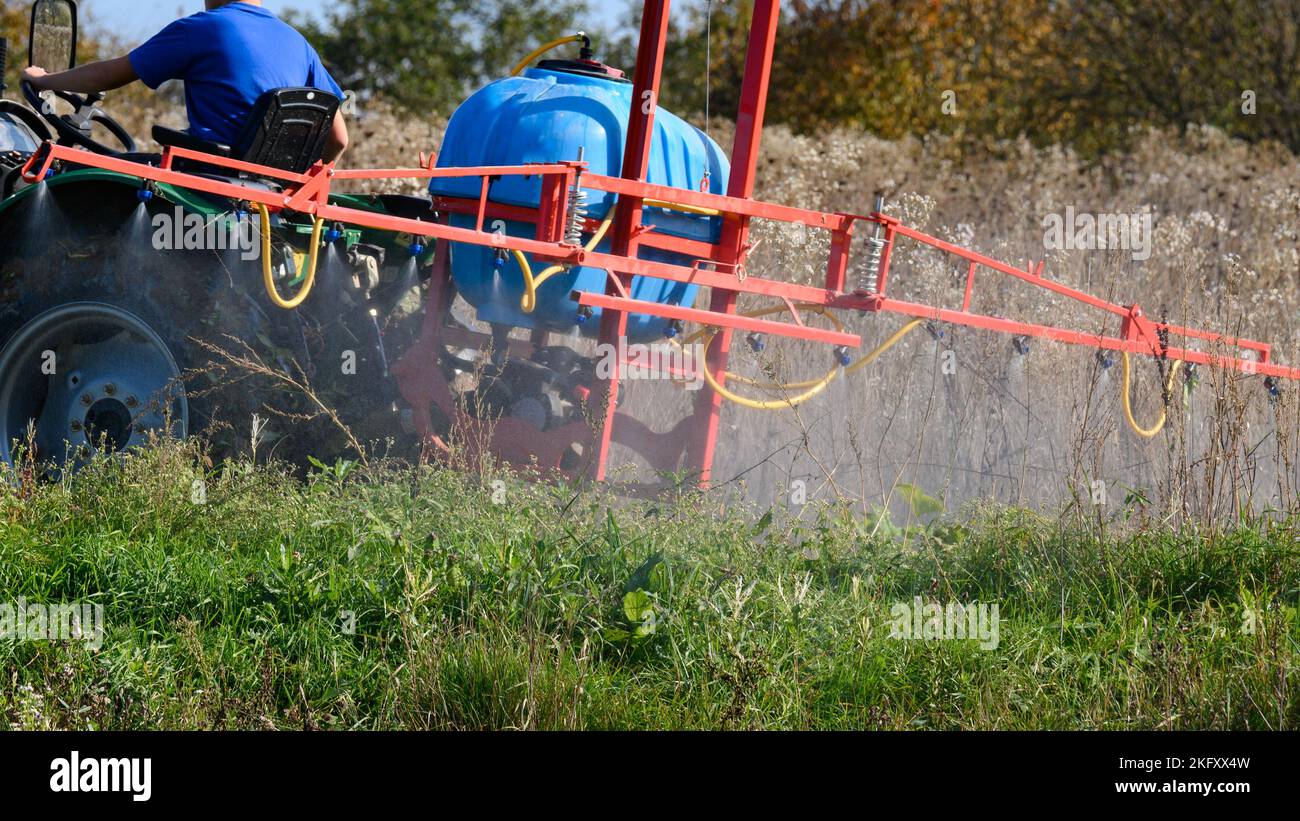 A small agricultural tractor is treating the field with herbicides against weeds, autumn ...