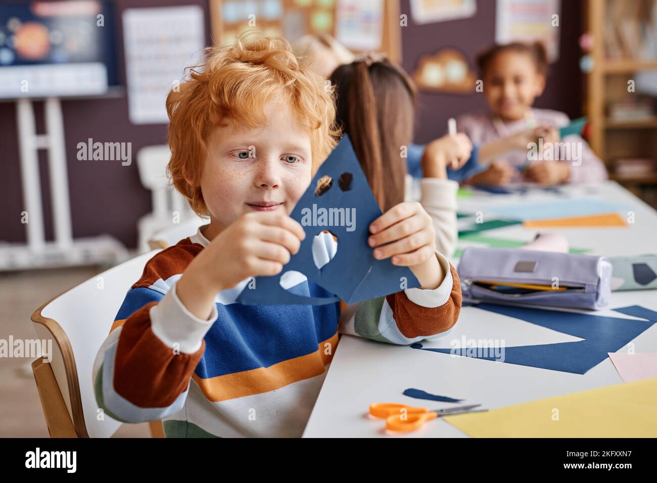 Cute primary school learner holding blue paper with holes for eyes and ...