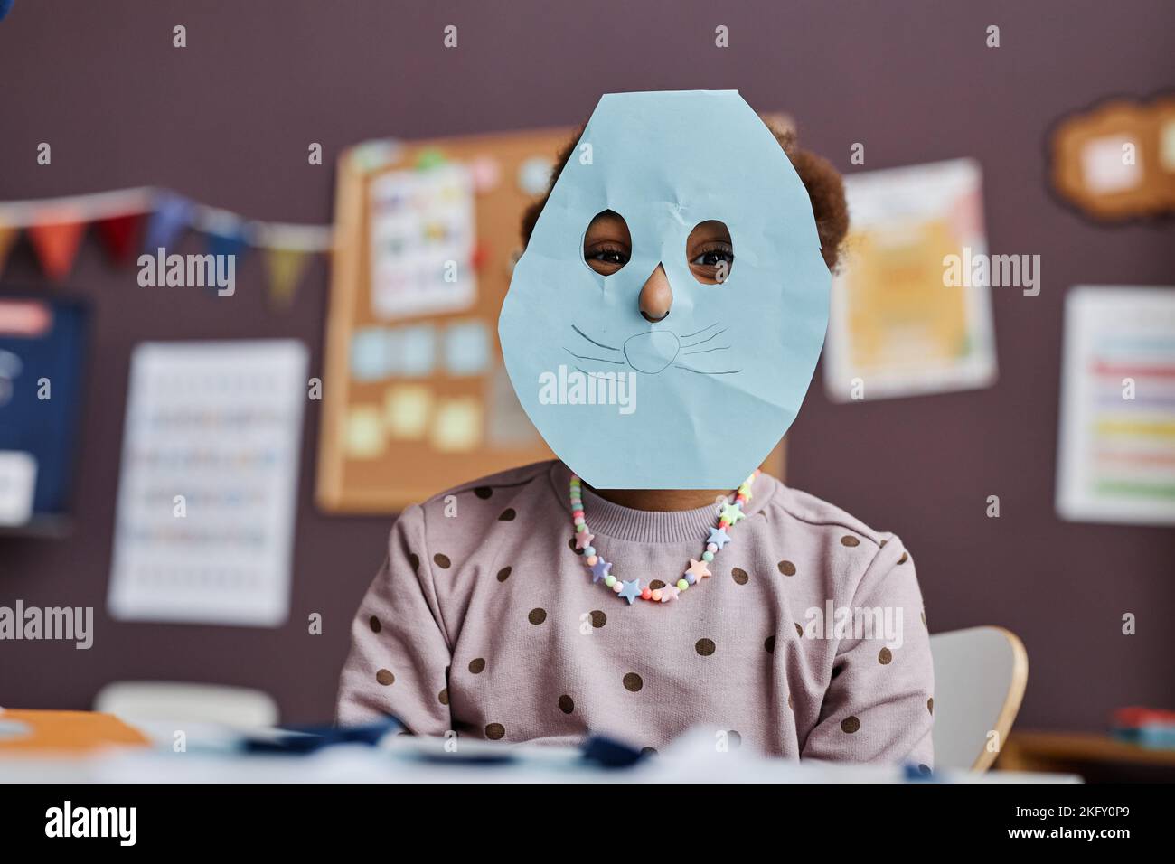 Cute little girl with blue paper mask on face sitting in front of ...