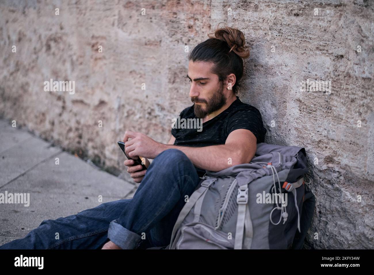 young caucasian man with long hair collected beard sitting on the floor ...