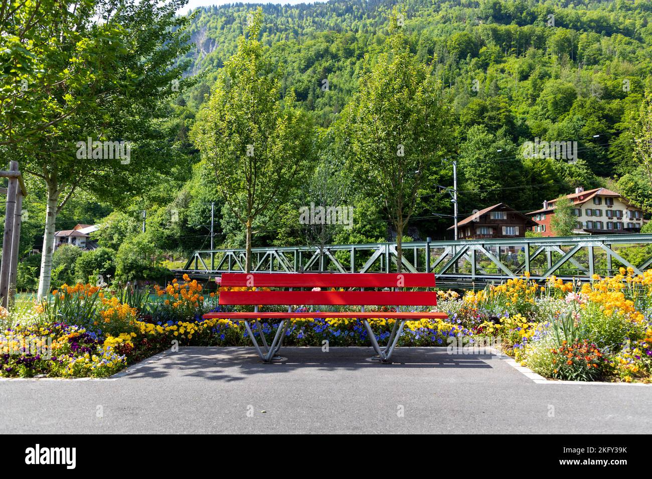 Red park bench surrounded by springtime flowers and forrest in the ...