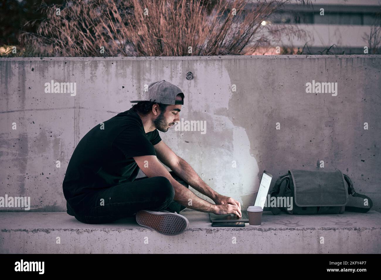 caucasian guy in gray cap black t-shirt sitting on the concrete floor ...