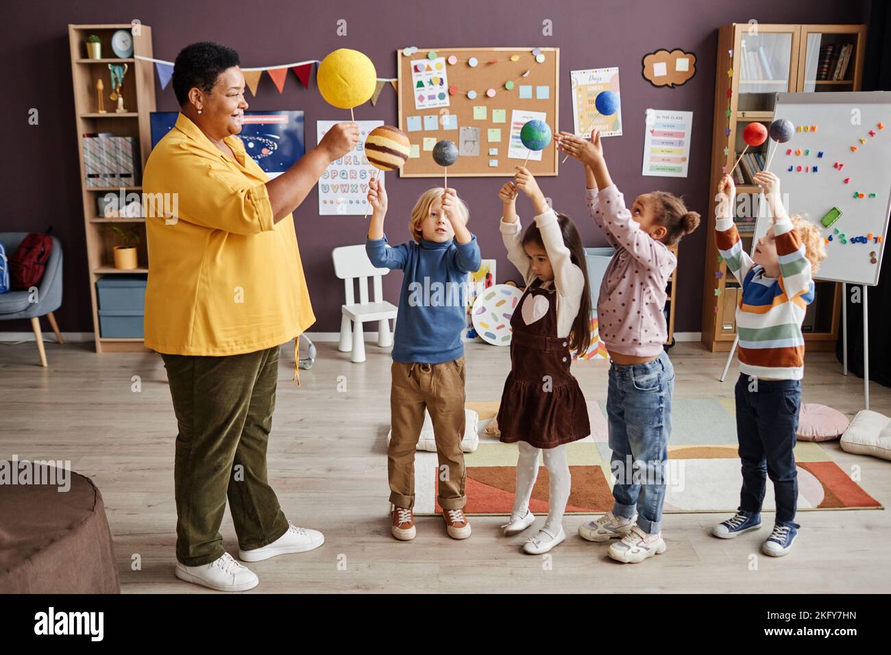 Mature teacher of nursery school and group of little kids with planet ...