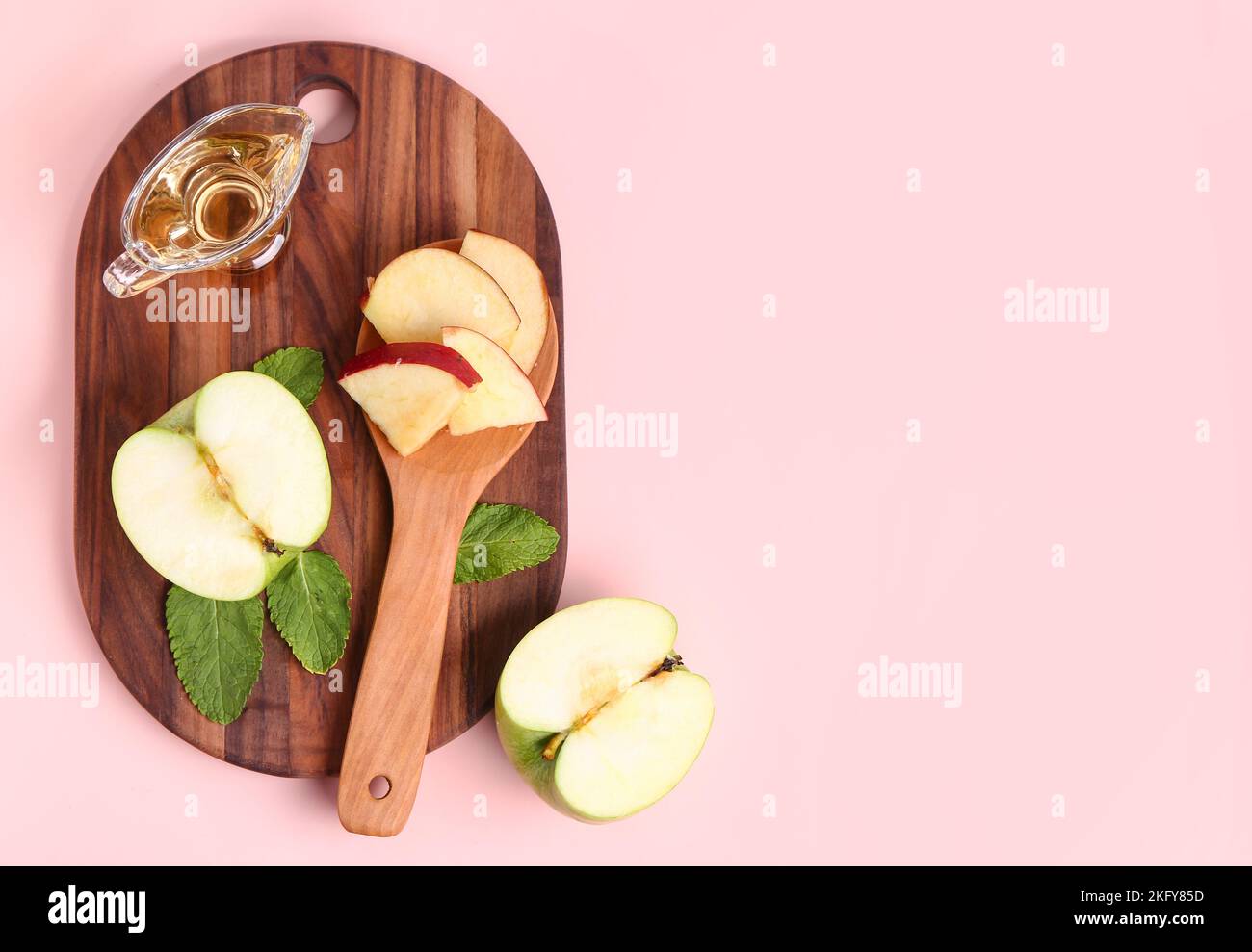 Wooden board with gravy boat of apple cider vinegar and fruits on pink ...